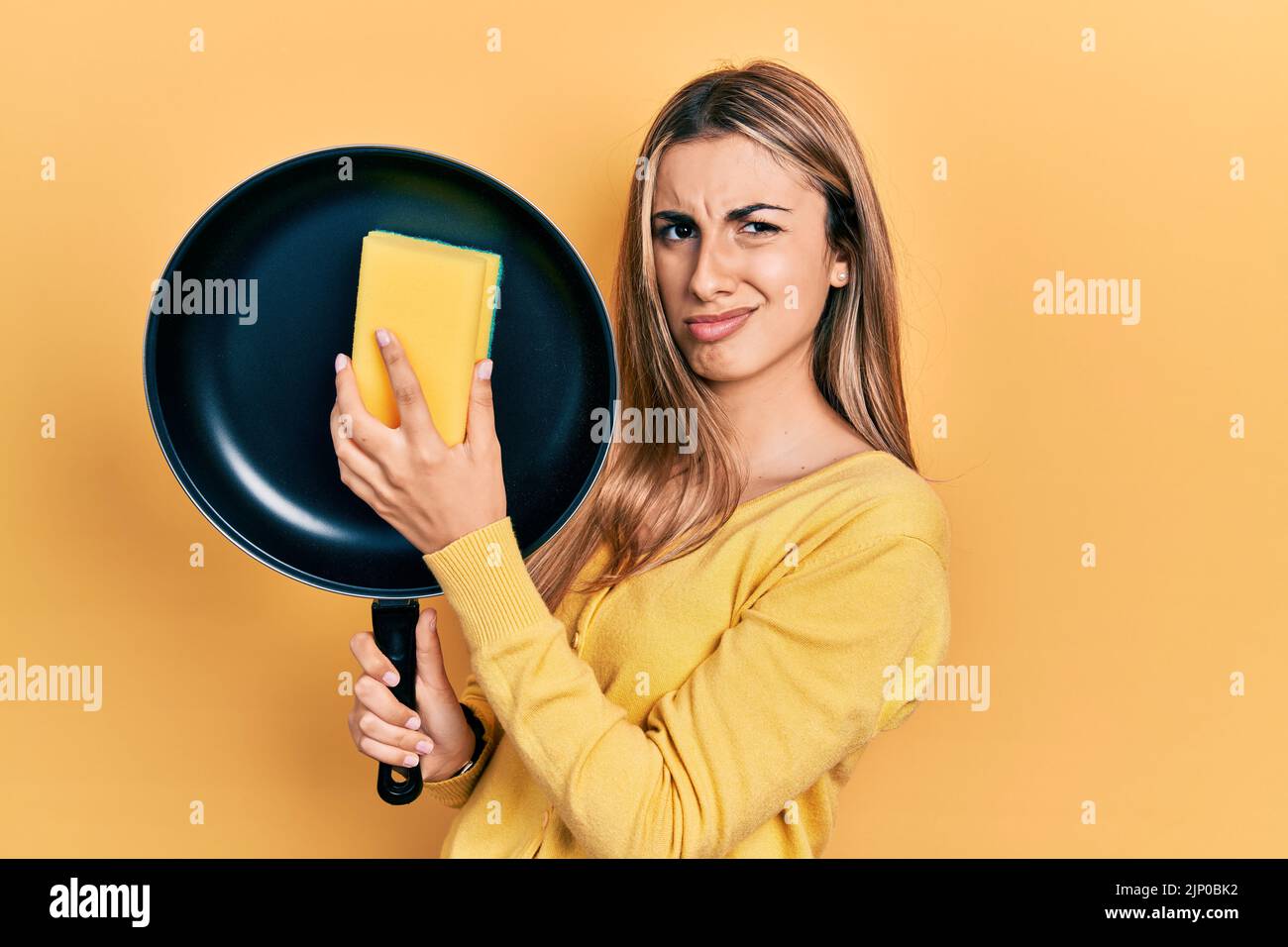 Beautiful hispanic woman cleaning cooking pan with scourer clueless and ...