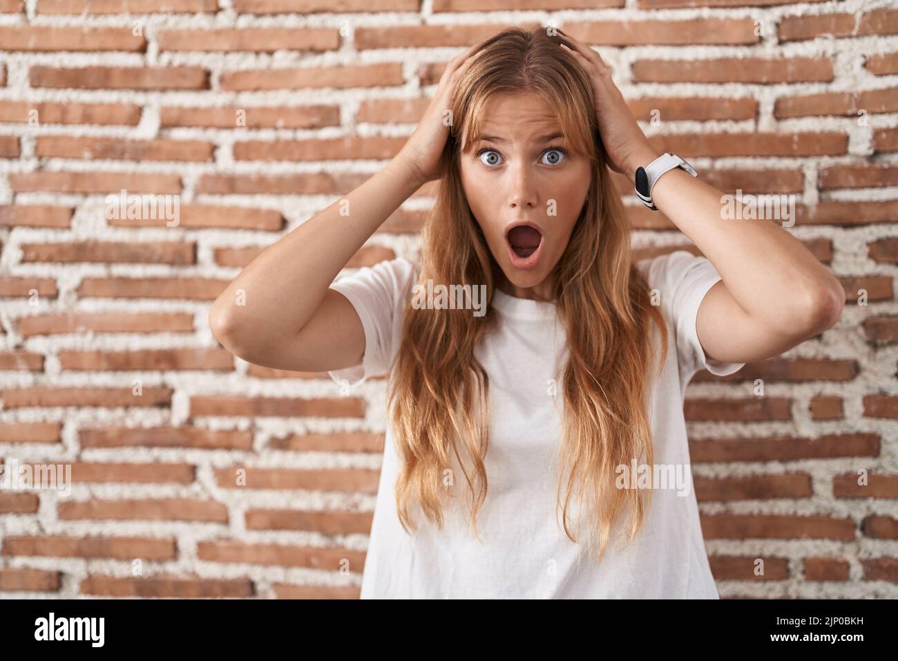 Young caucasian woman standing over bricks wall crazy and scared with ...