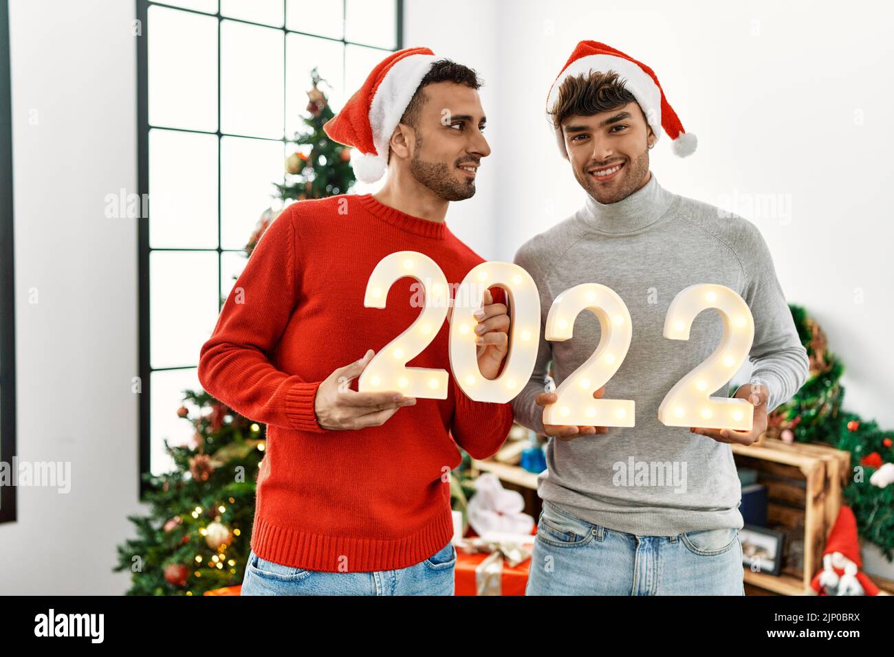 Two hispanic men couple celebrate new year 2022 standing by christmas tree at home Stock Photo ...