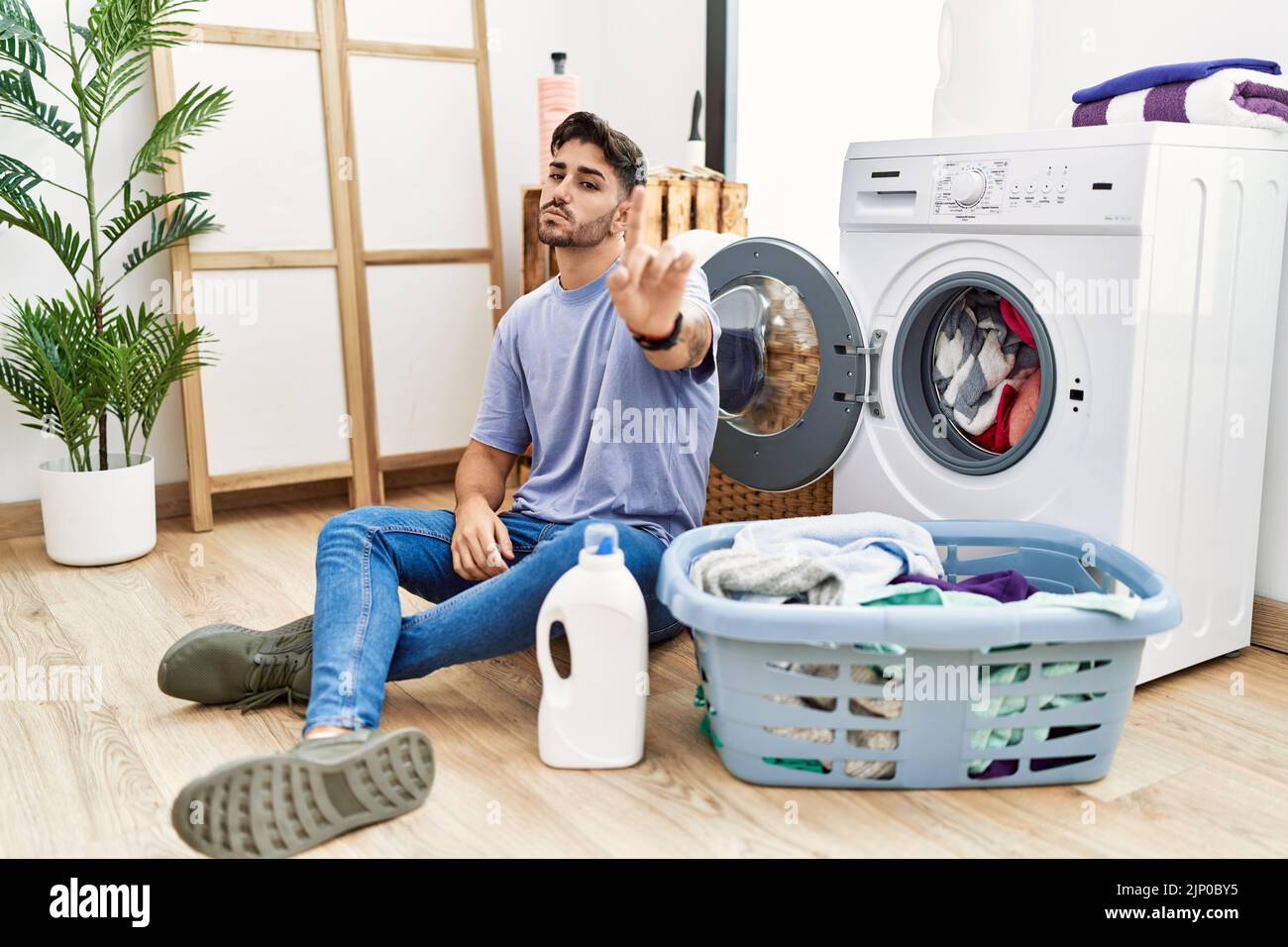 Young hispanic man putting dirty laundry into washing machine pointing ...