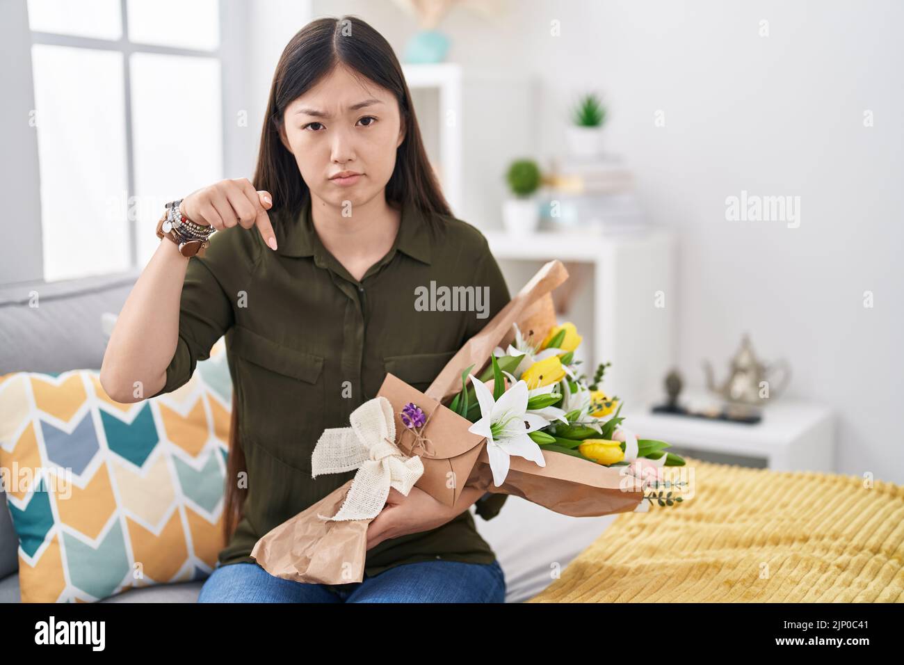Chinese young woman holding bouquet of white flowers pointing down ...