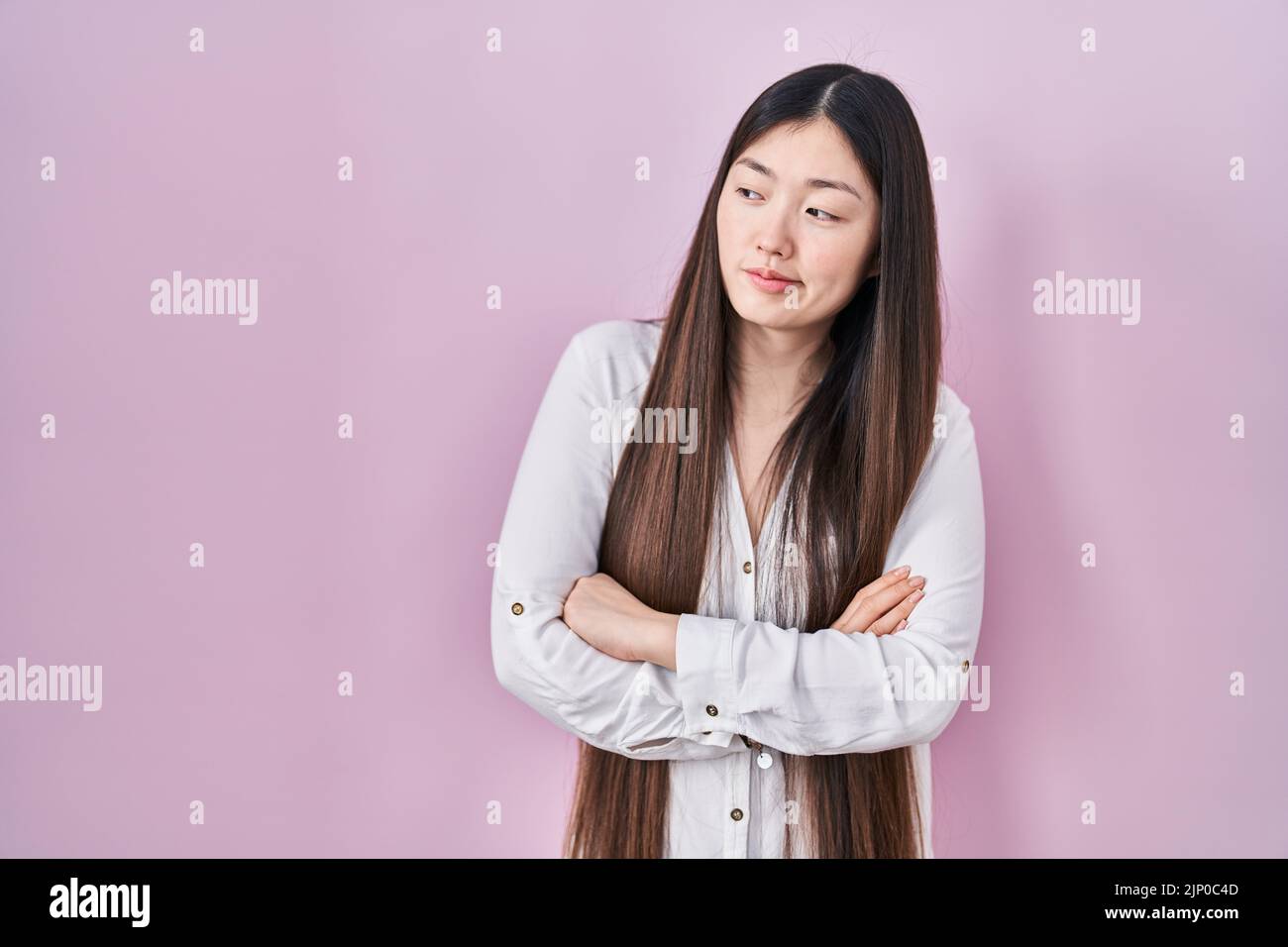 Chinese young woman standing over pink background looking to the side ...
