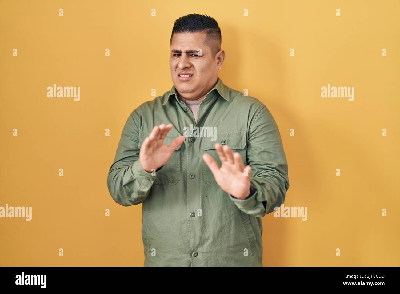 Hispanic young man standing over yellow background disgusted expression ...