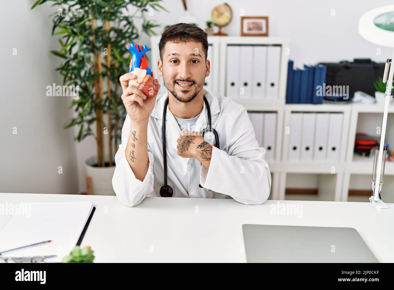 Young doctor holding heart at medical clinic pointing finger to one ...