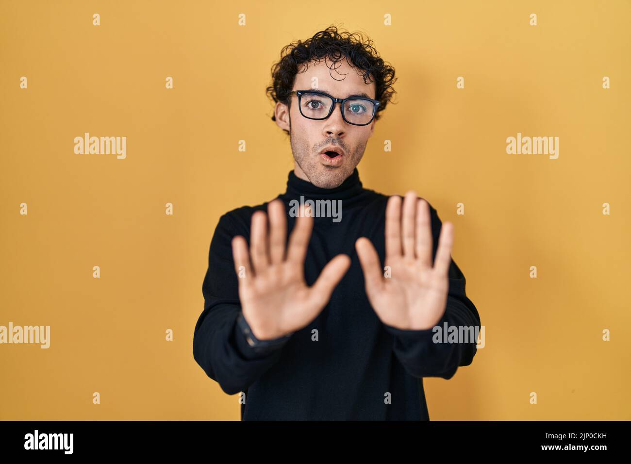 Hispanic man standing over yellow background moving away hands palms ...