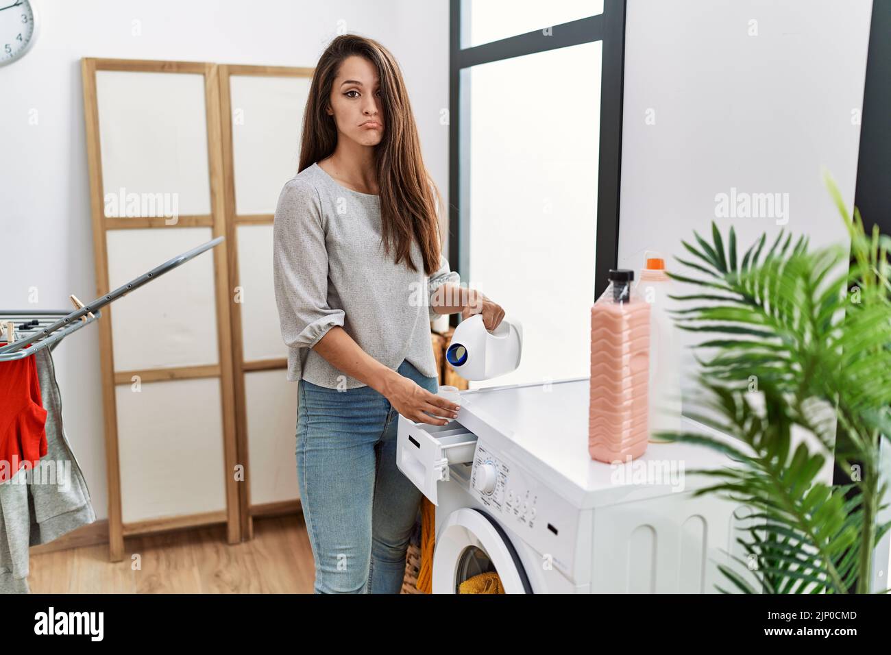 Young brunette woman putting detergent in washing machine depressed and ...