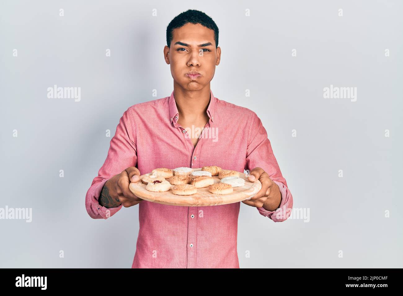Young african american guy holding tray with cake sweets puffing cheeks ...