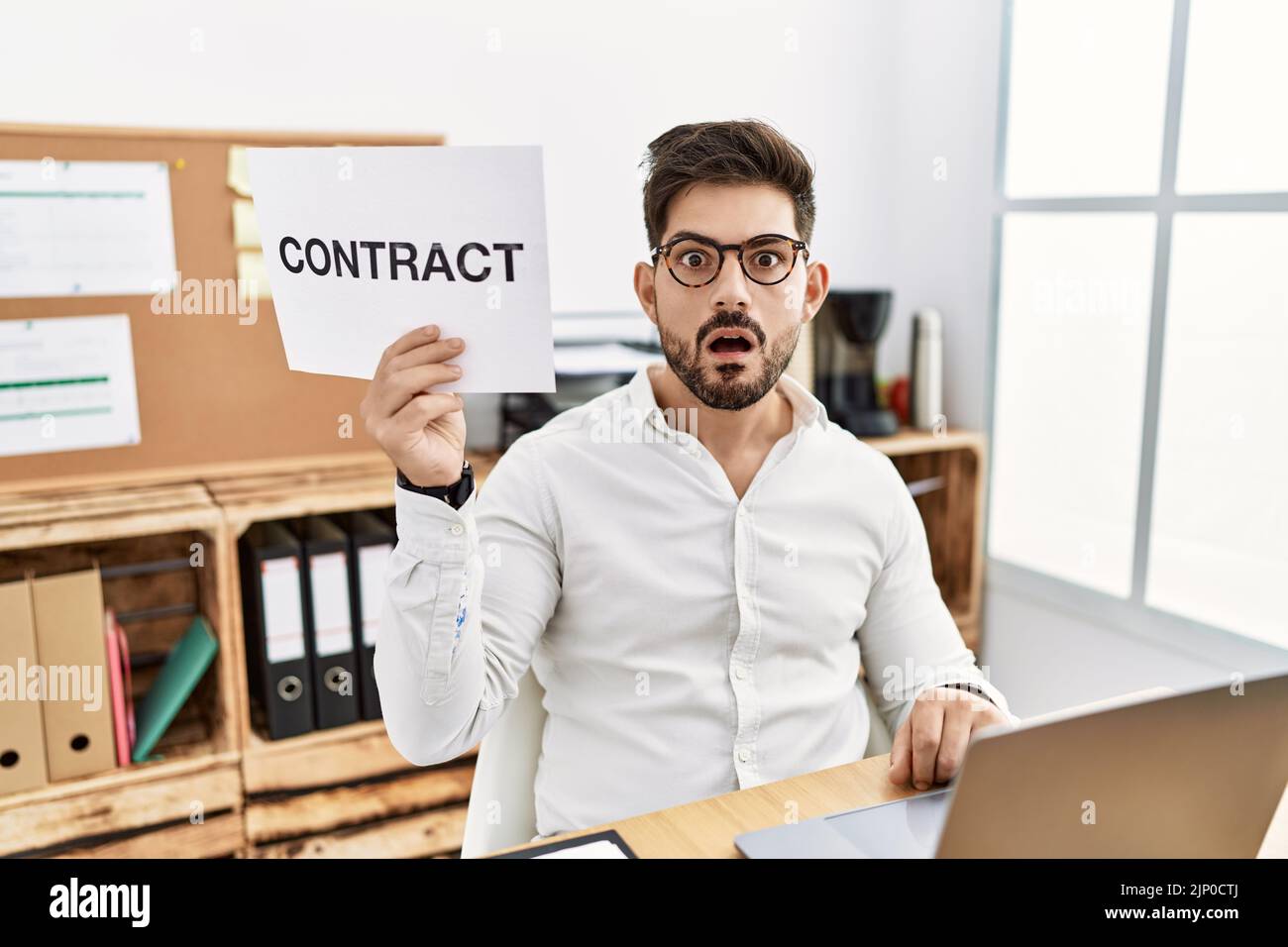 Young man with beard holding contract paper at the office scared and ...