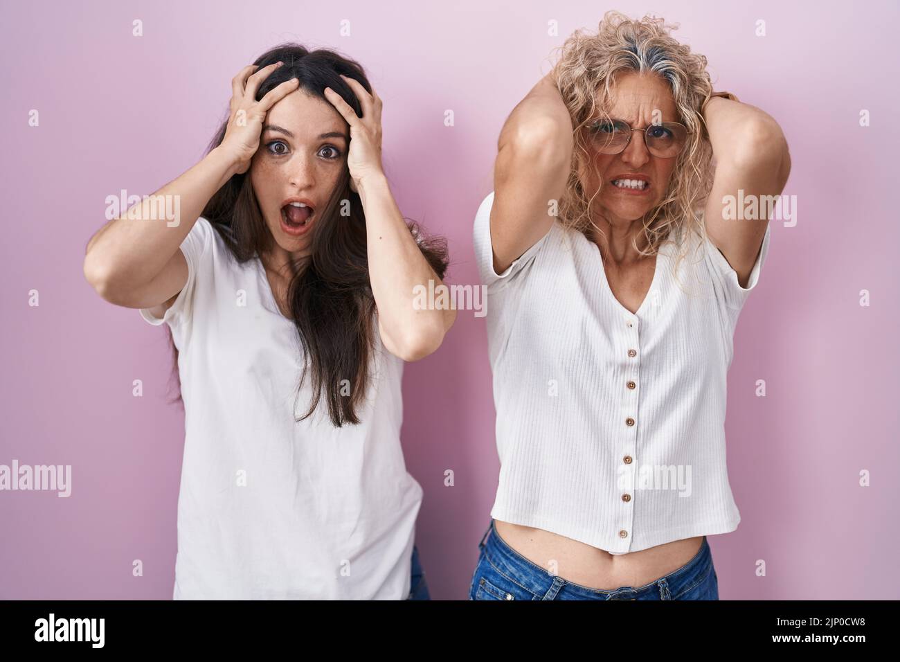 Mother and daughter standing together over pink background crazy and ...