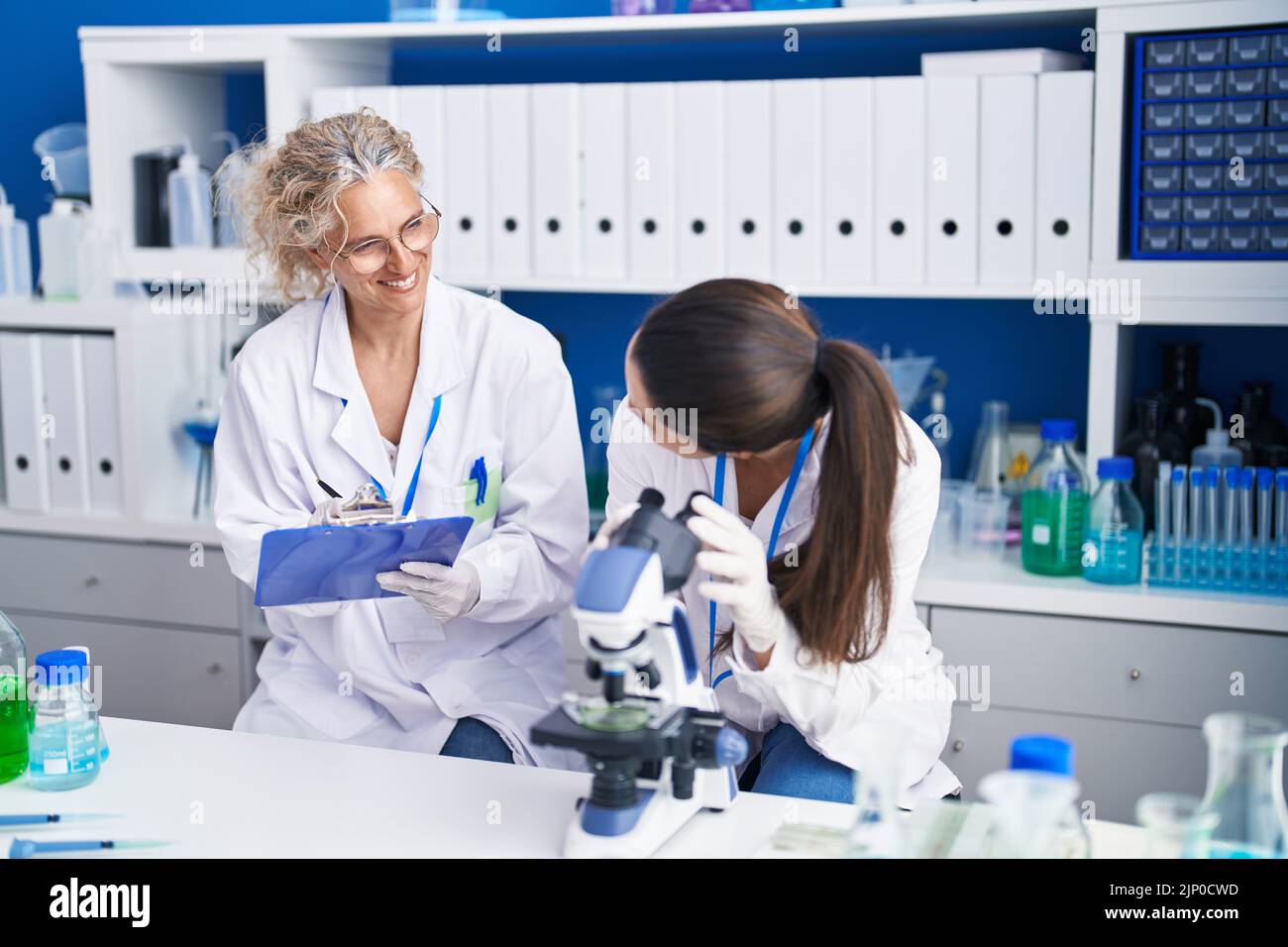 Two women scientists using microscope write on document at laboratory ...