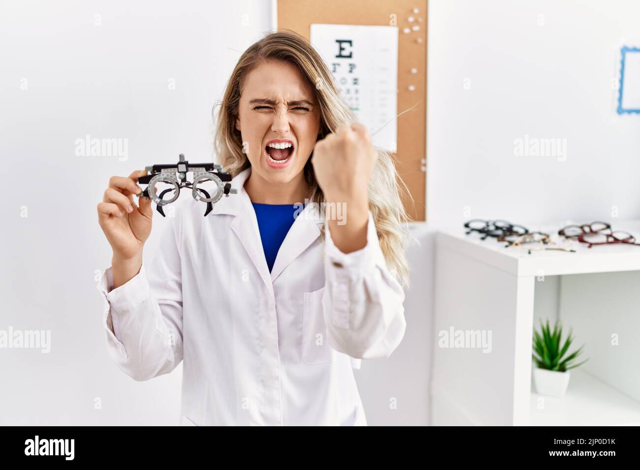 Young beautiful optician woman holding optometry glasses annoyed and ...