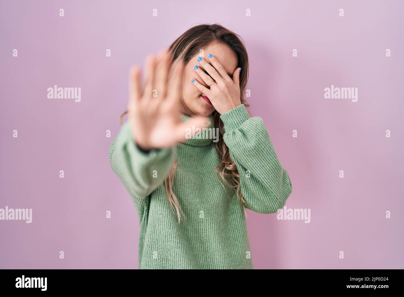 Young caucasian woman standing over pink background covering eyes with ...