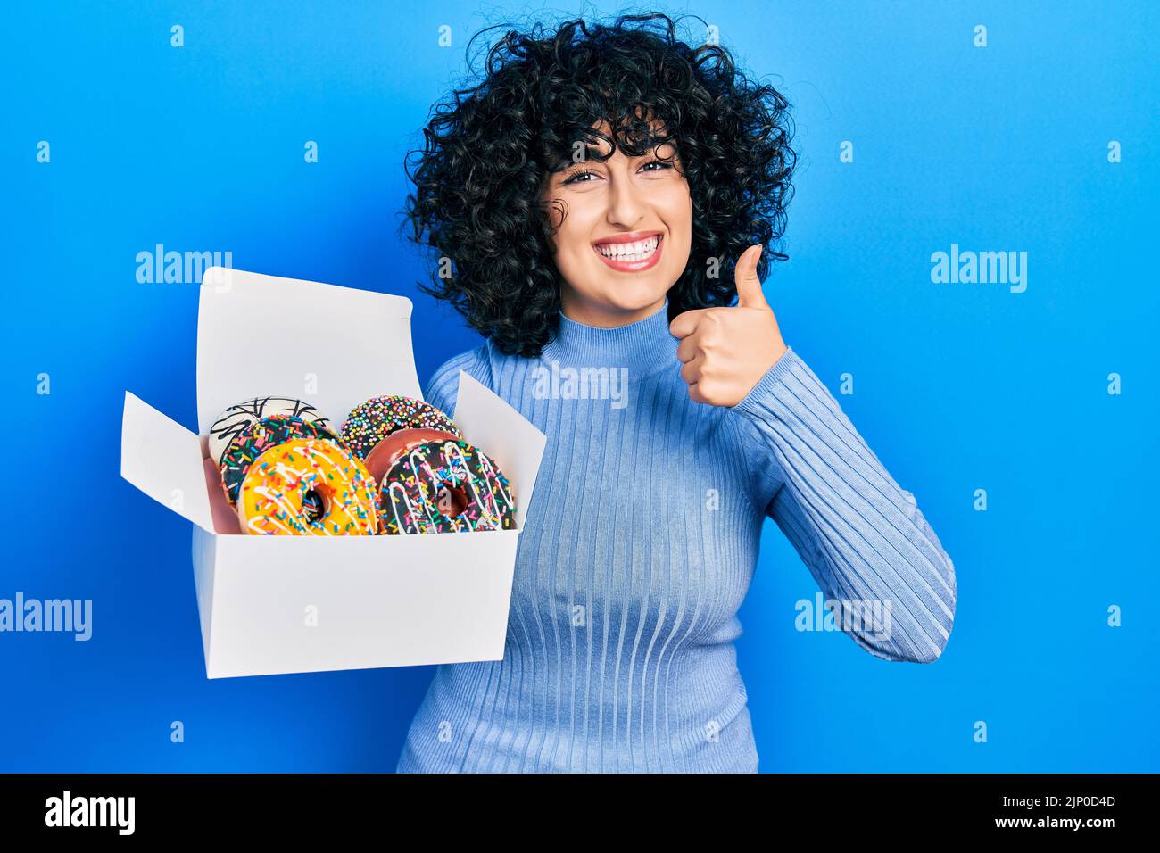 Young middle east woman holding tasty colorful doughnuts box smiling ...