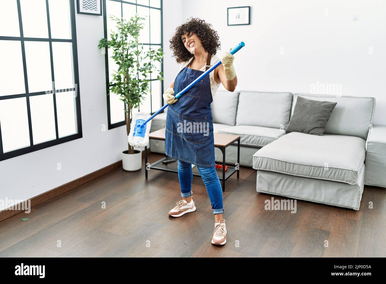 Young middle east woman cleaning and using mop as a guitar at home ...