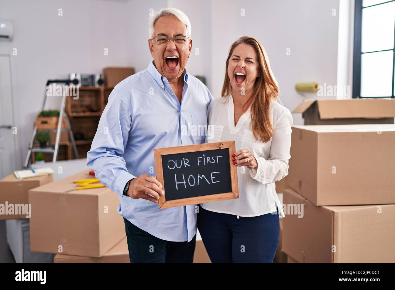 Middle age hispanic couple moving to a new home holding banner angry ...