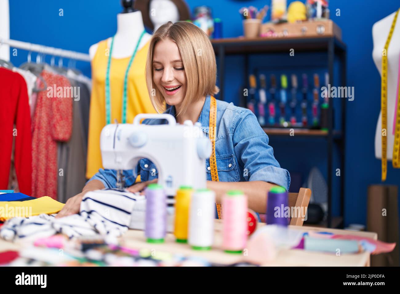 Young blonde woman tailor smiling confident using sewing machine at ...