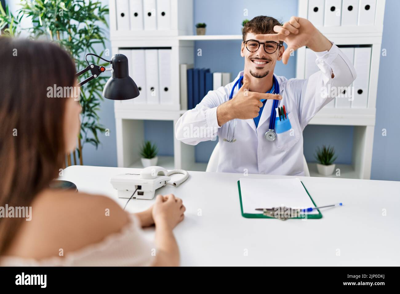 Young doctor with client at medical clinic smiling making frame with ...