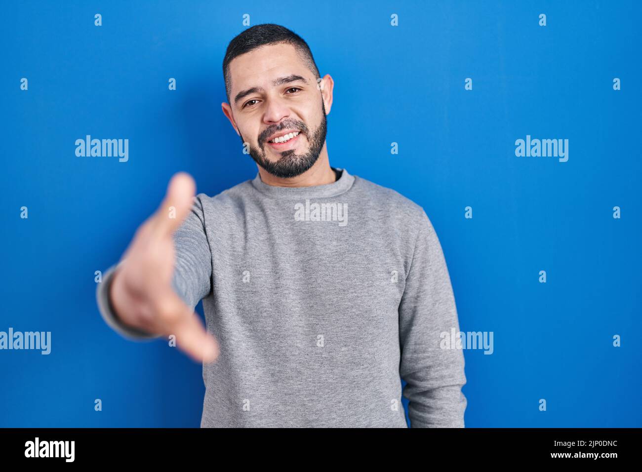 Hispanic man standing over blue background smiling friendly offering ...