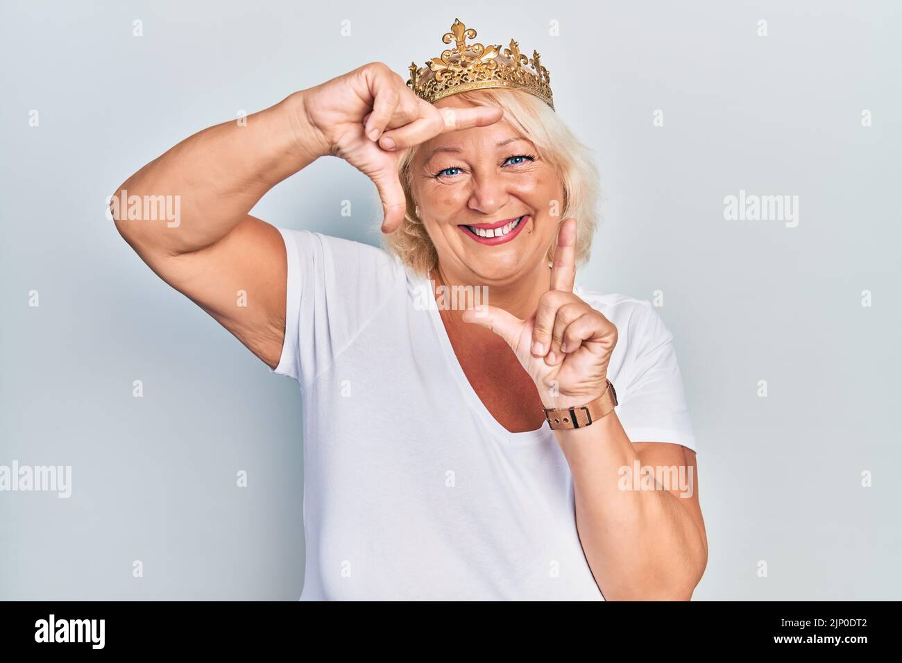 Middle age blonde woman wearing queen crown smiling making frame with ...
