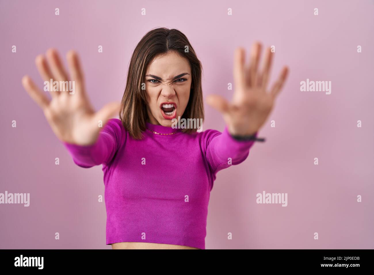 Hispanic woman standing over pink background doing stop gesture with ...