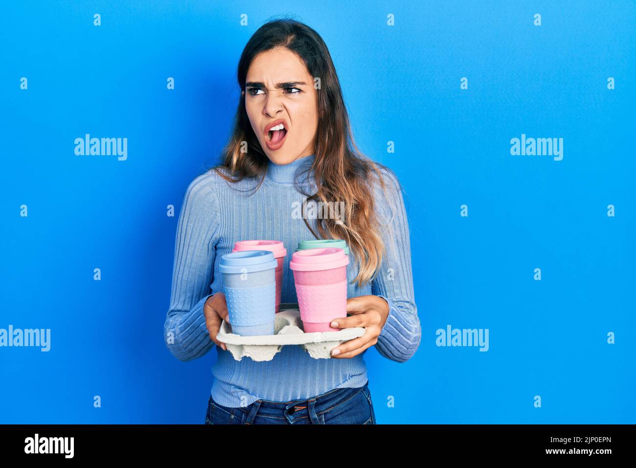 Young hispanic girl holding tray with take away coffee angry and mad ...