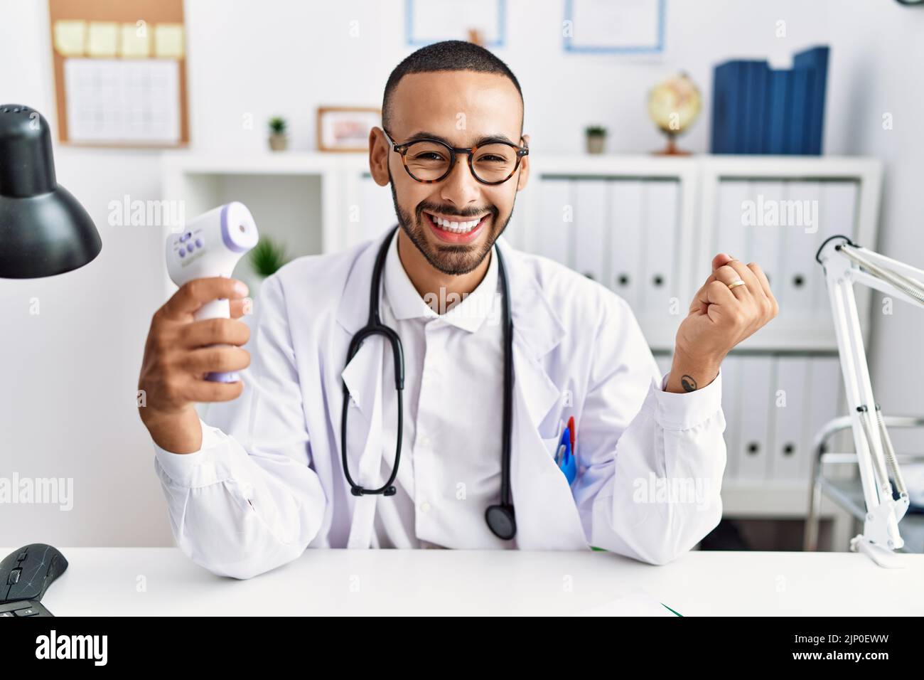 African american doctor man holding thermometer at the clinic screaming ...