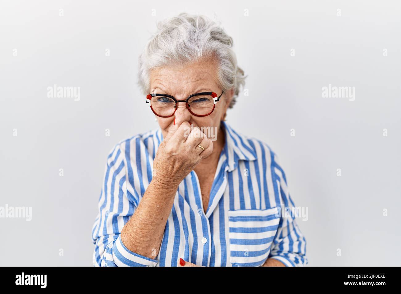 Senior woman with grey hair standing over white background smelling ...