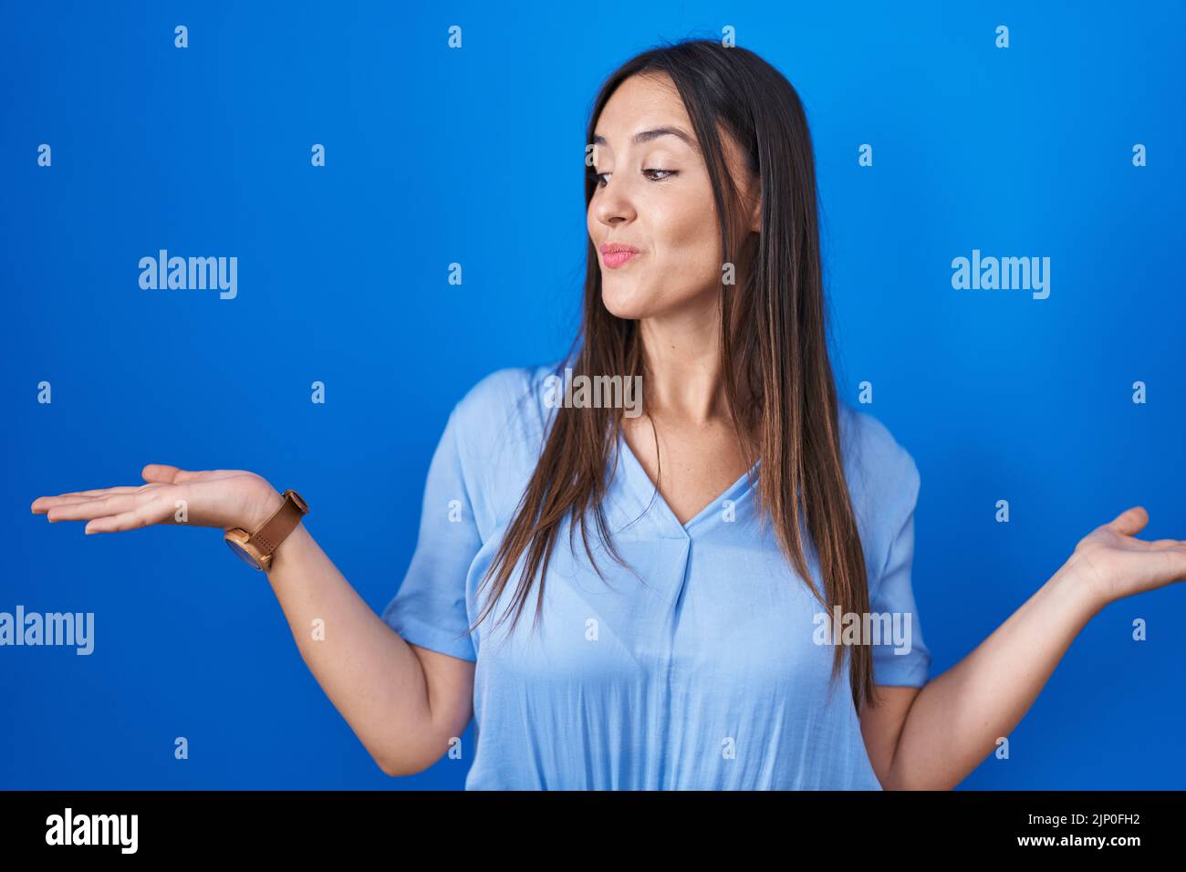 Young brunette woman standing over blue background smiling showing both ...