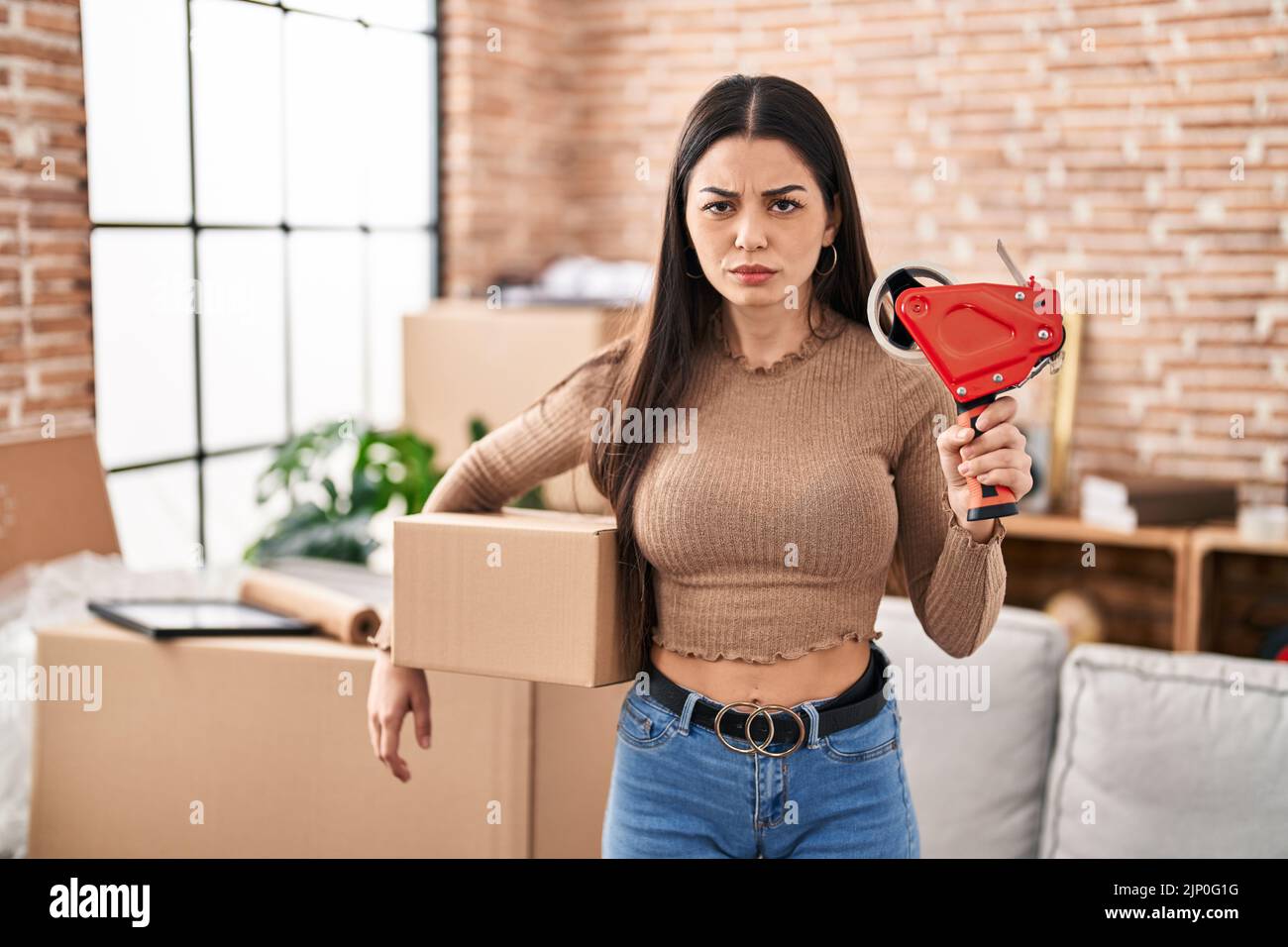 Young woman moving to a new home packing boxes depressed and worry for ...