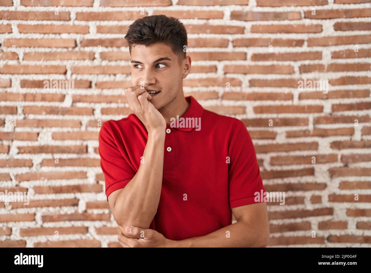 Young hispanic man standing over bricks wall looking stressed and ...