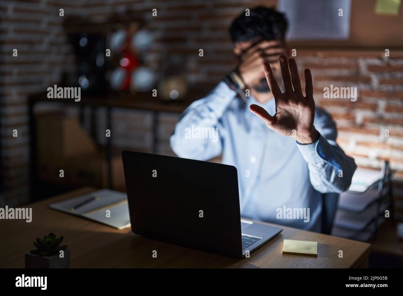 Young hispanic man with beard working at the office at night covering ...