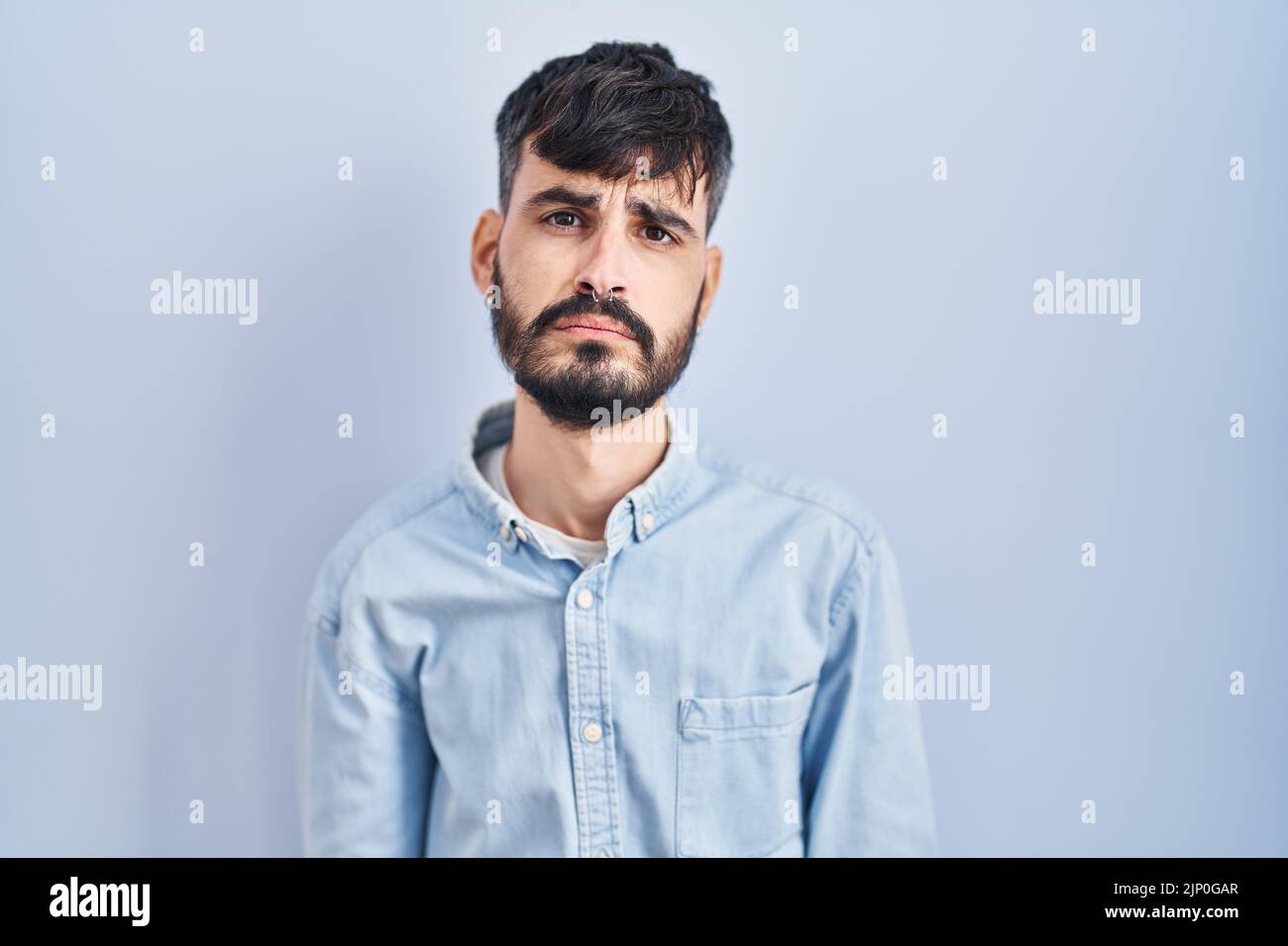 Young hispanic man with beard standing over blue background depressed ...
