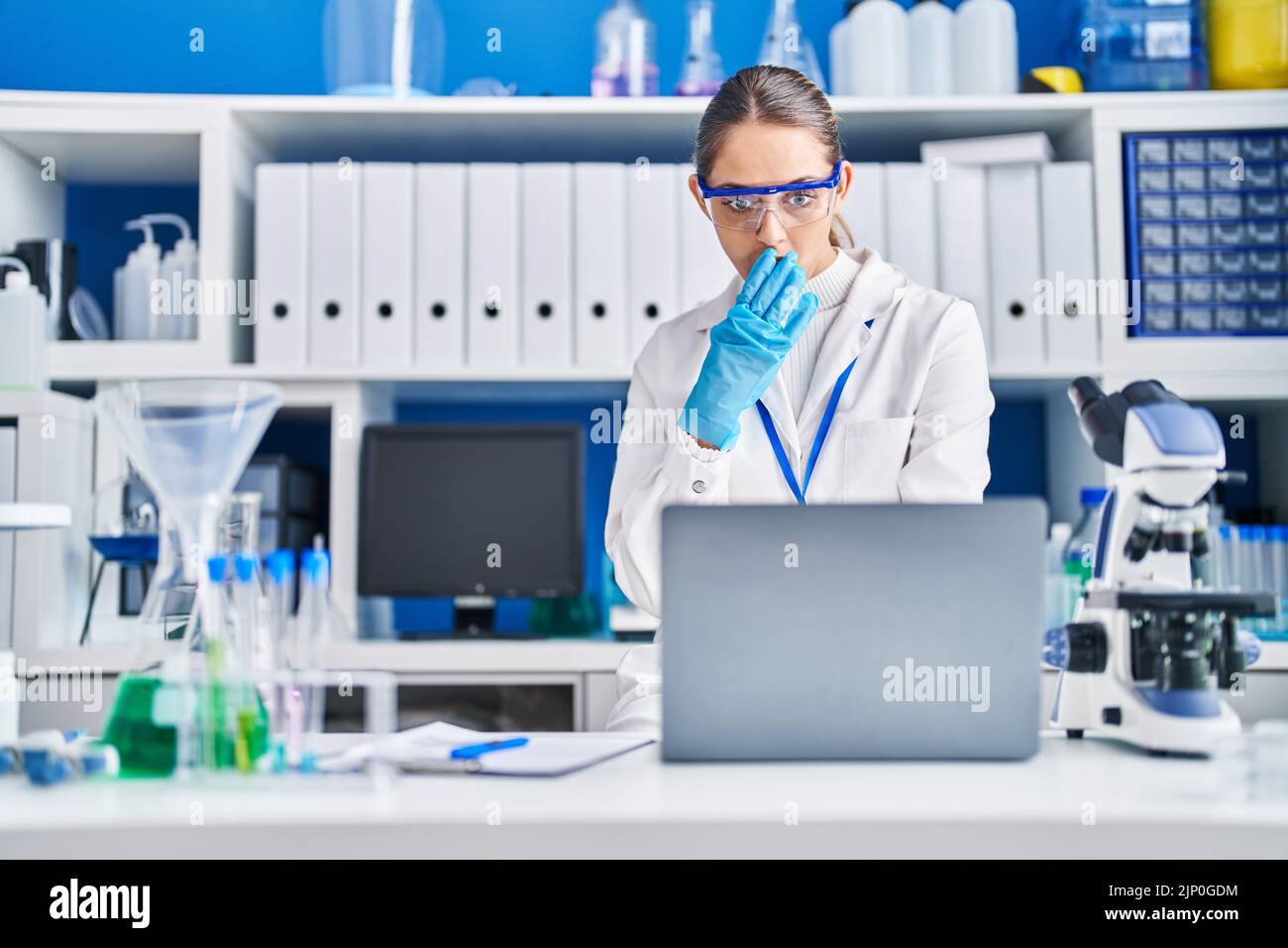 Young blonde woman working at scientist laboratory covering mouth with ...