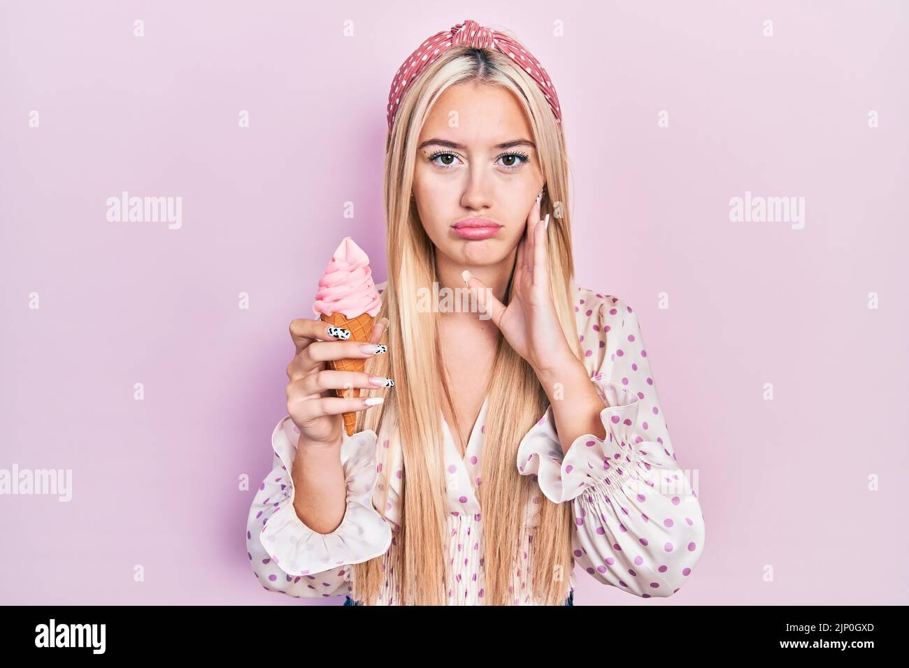 Young blonde girl holding ice cream depressed and worry for distress ...