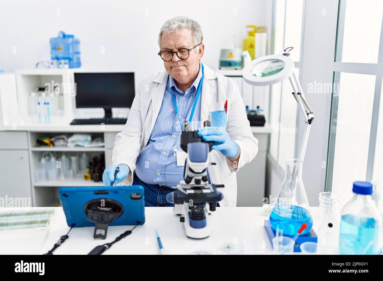Middle age grey-haired man wearing scientist uniform using microscope ...