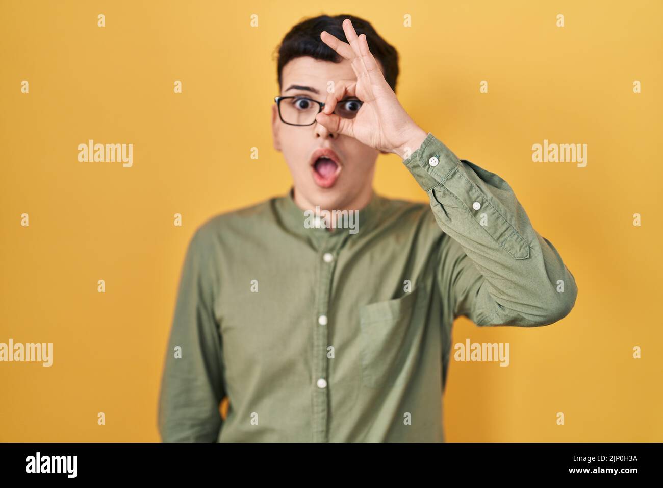 Non binary person standing over yellow background doing ok gesture ...