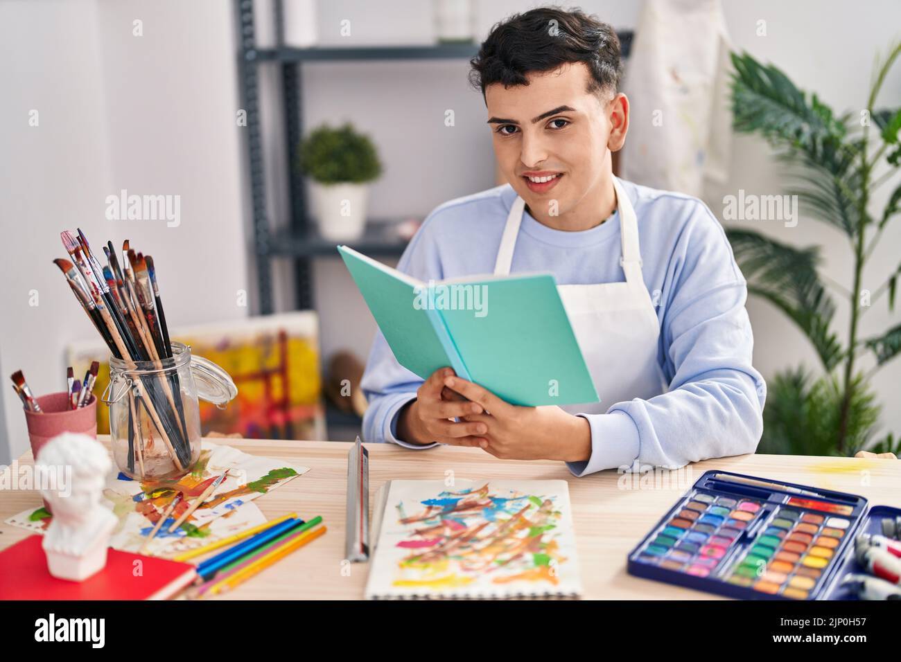 Young non binary man artist smiling confident reading book at art ...