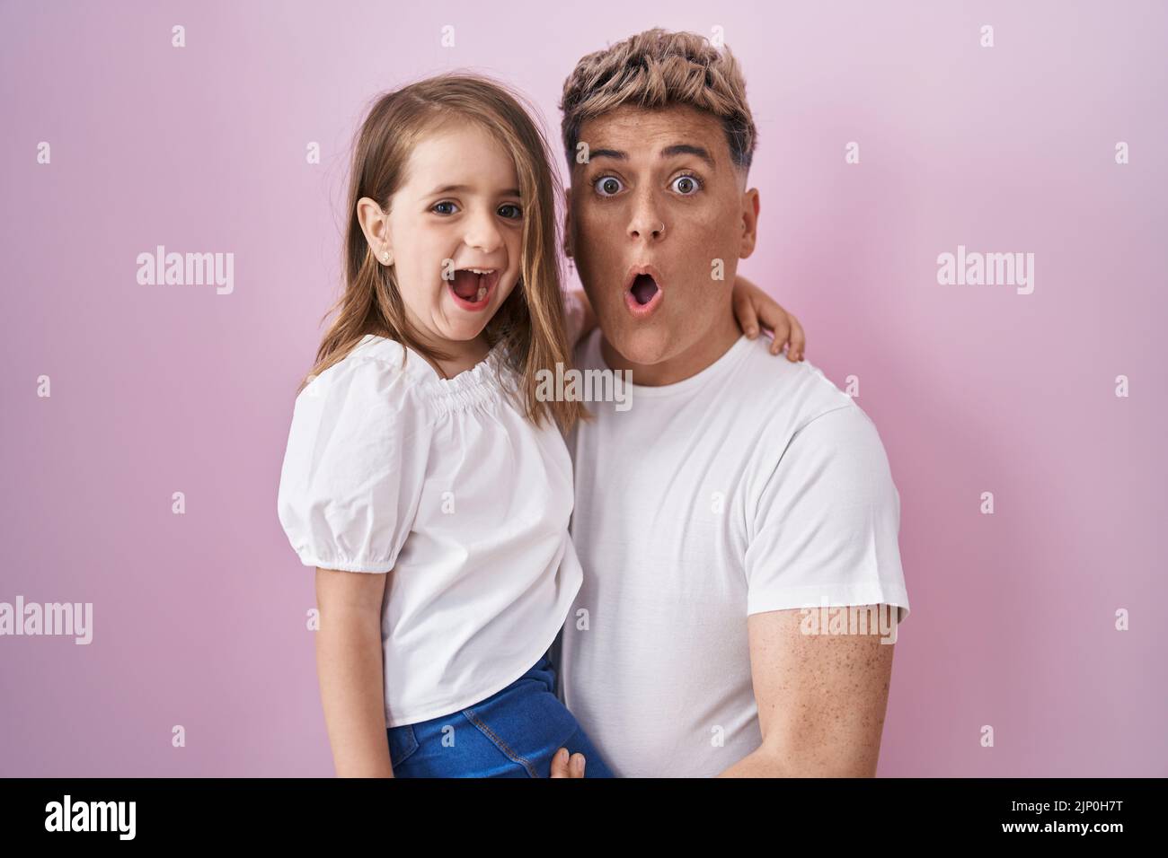 Young father hugging daughter over pink background scared and amazed ...