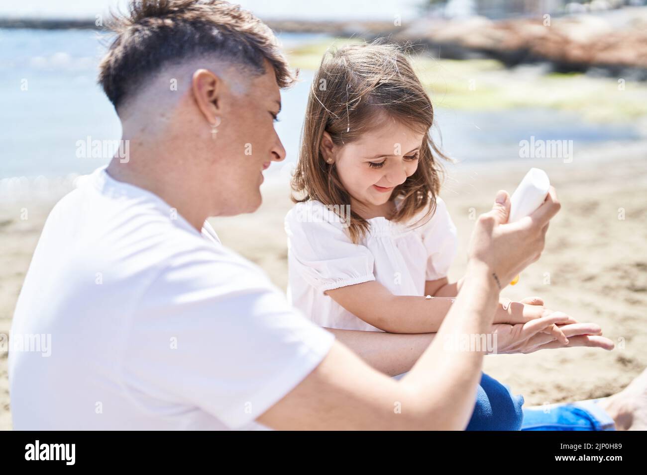 Father and daughter applying sunscreen sitting on sand at beach Stock Photo - Alamy
