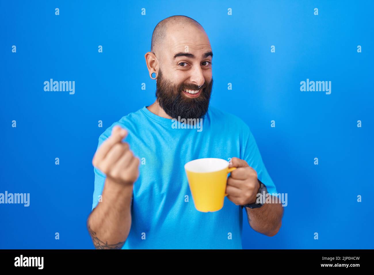 Young hispanic man with beard and tattoos drinking a cup of coffee ...