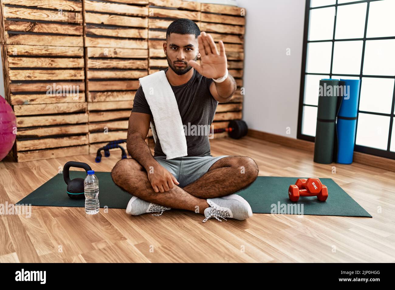 Young indian man sitting on training mat at the gym doing stop sing ...