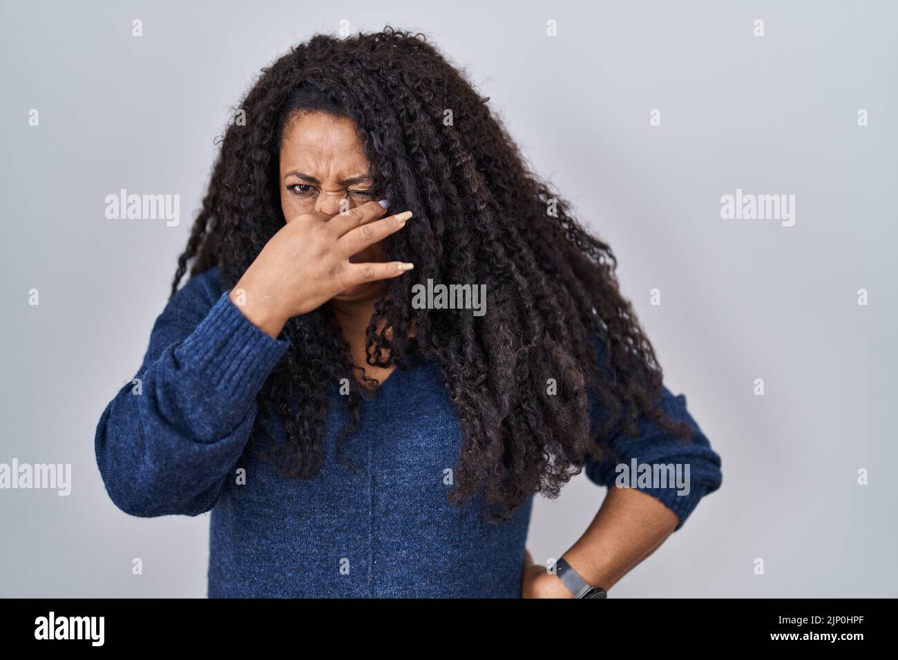 Plus size hispanic woman standing over white background smelling ...
