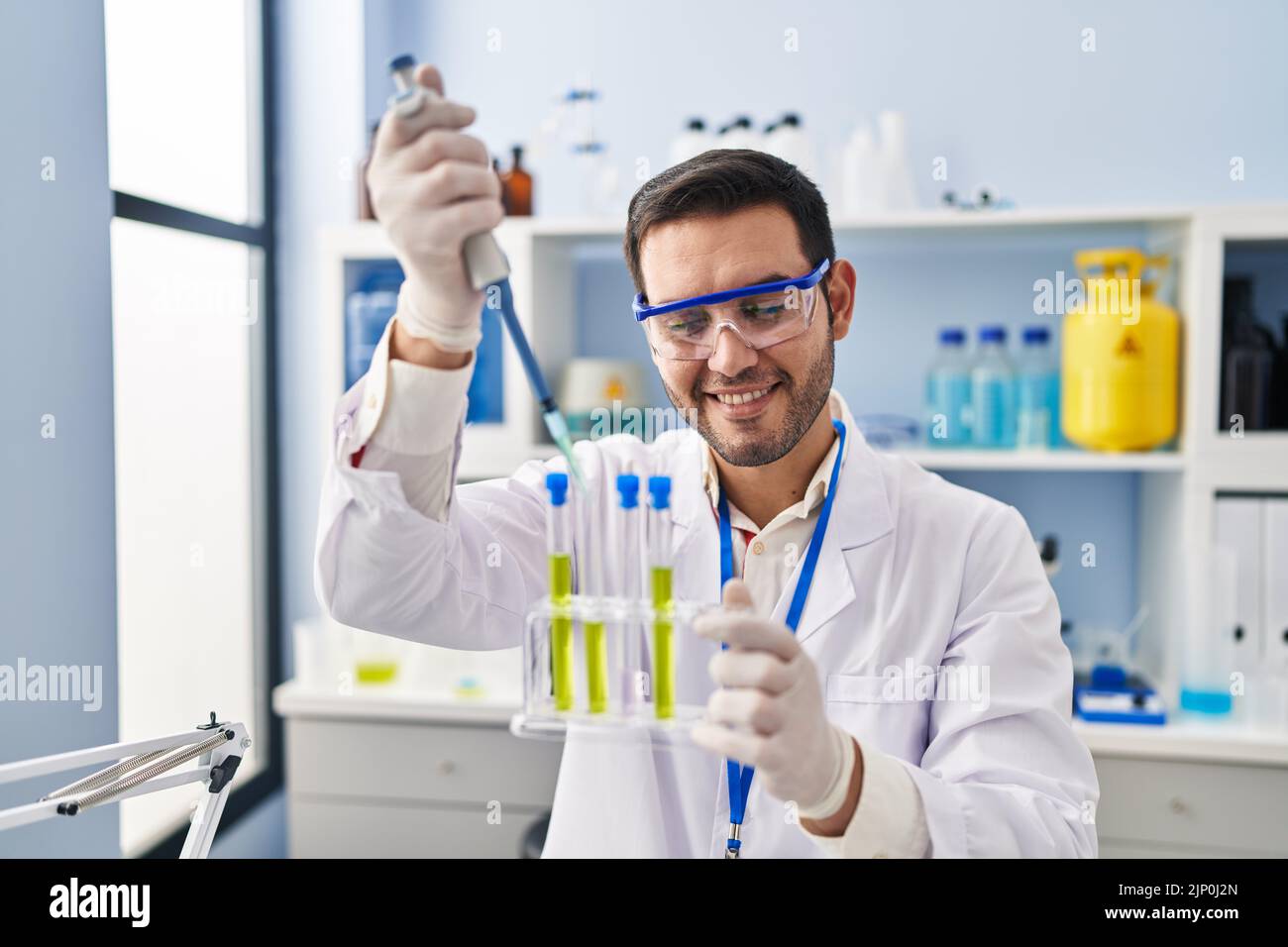 Young hispanic man scientist measuring liquid using pipette at ...