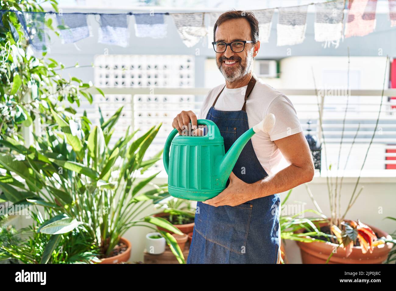 Middle age man wearing gardener apron holding watering can at home ...