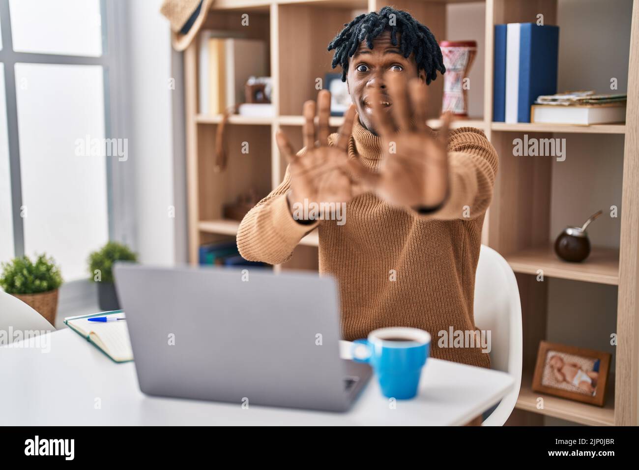 Young african man with dreadlocks working using computer laptop afraid ...