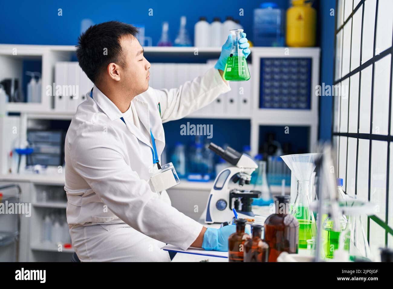 Young chinese man wearing scientist uniform measuring liquid at ...