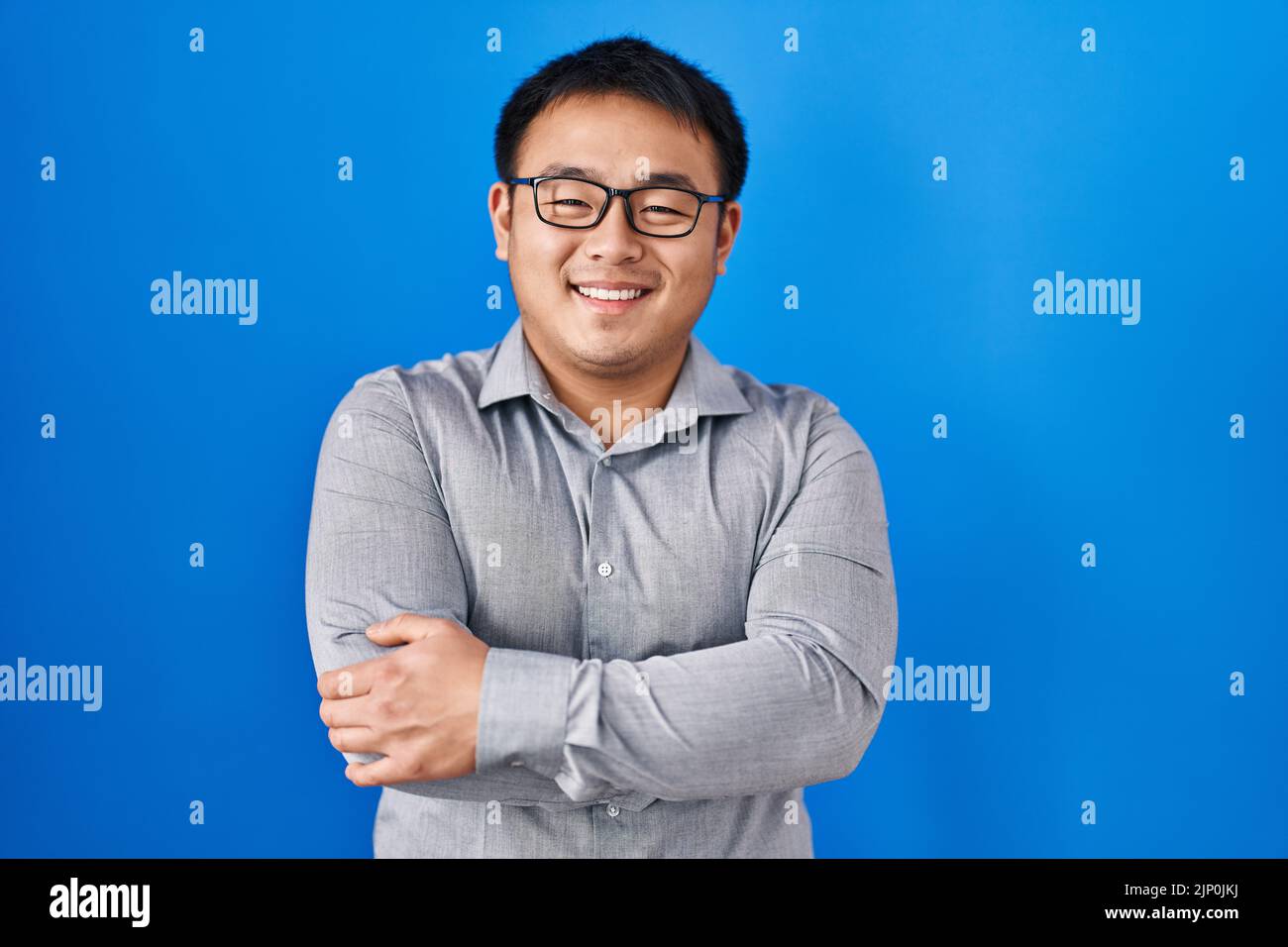 Young chinese man standing over blue background happy face smiling with ...