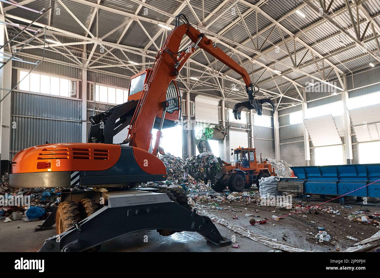 Grabbing excavator collects garbage in plant warehouse Stock Photo - Alamy
