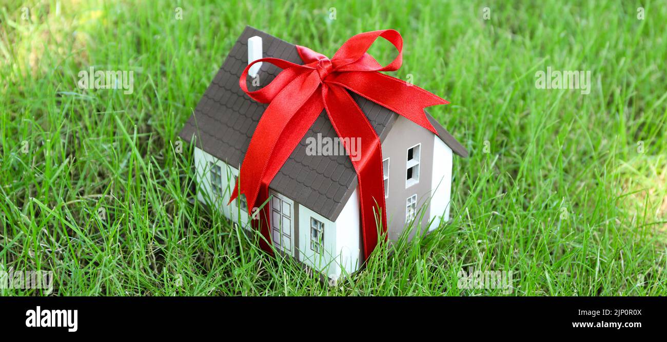 House model with red ribbon on green lawn Stock Photo - Alamy