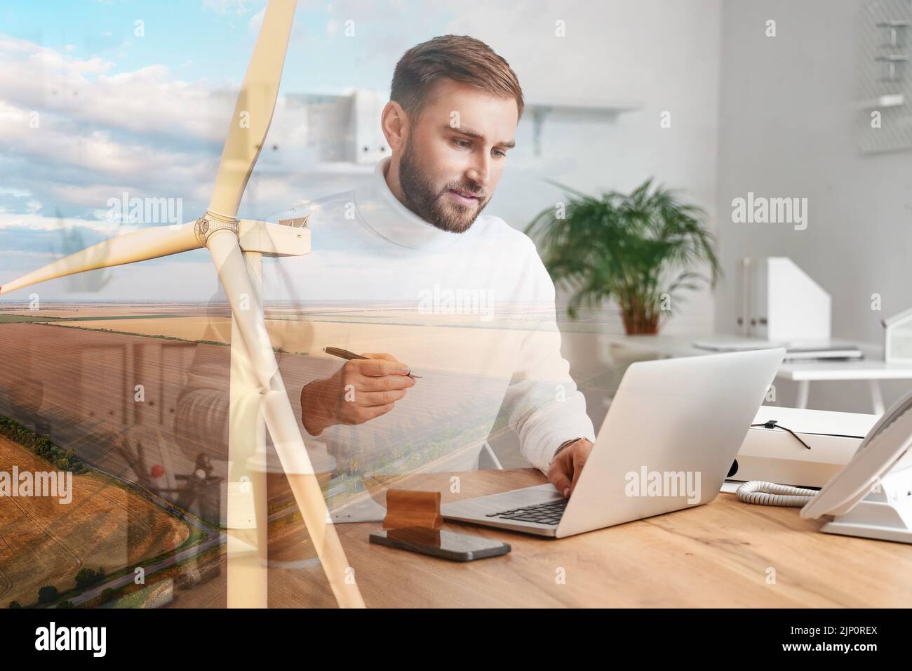 Double exposure of businessman using laptop in office and windmills for ...